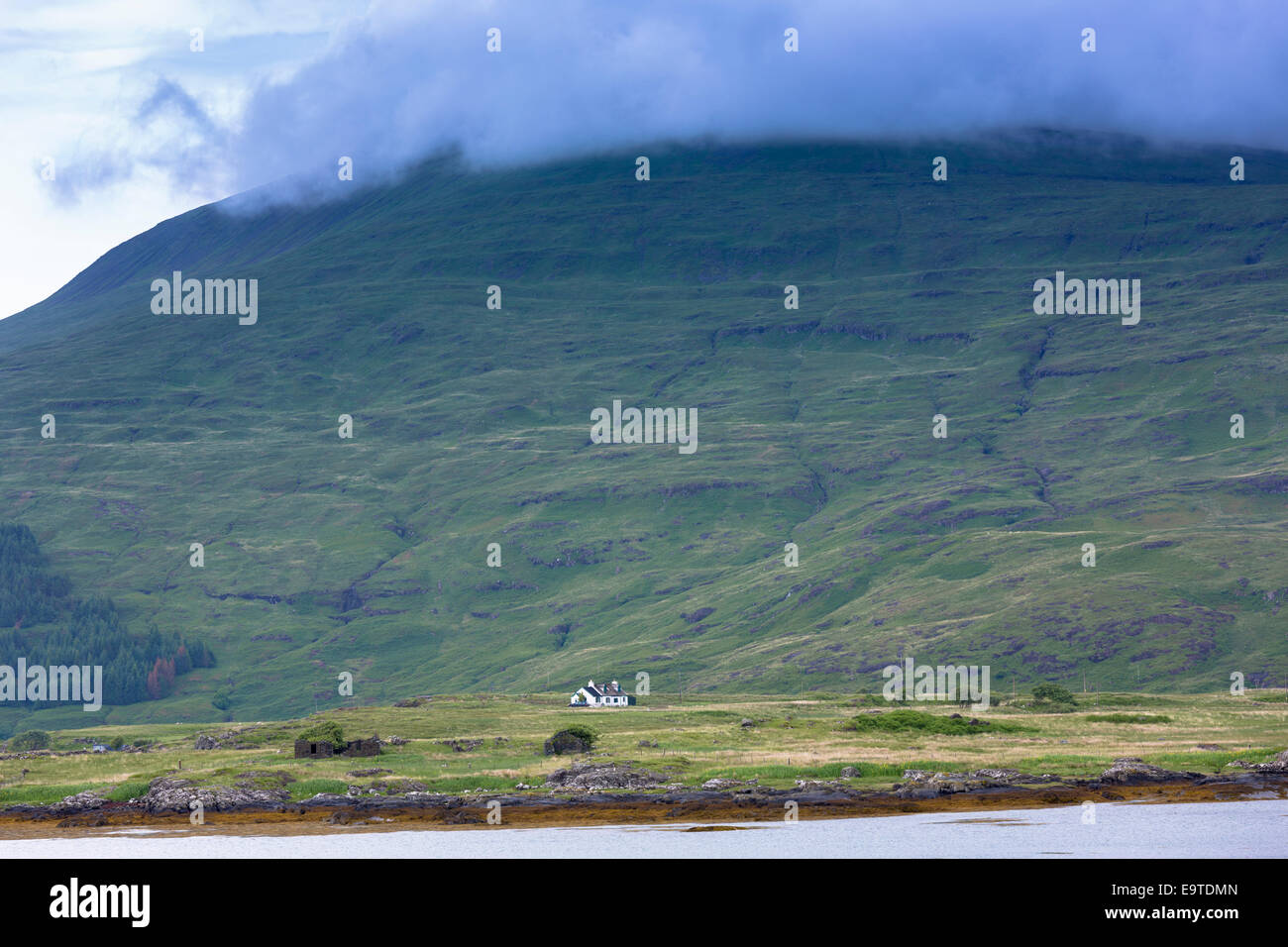 Small white solitary crofters cottage nestling below mountain range by ...
