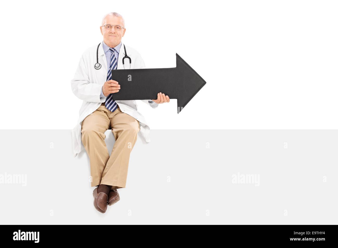 Mature doctor holding an arrow and sitting on a panel isolated on white ...