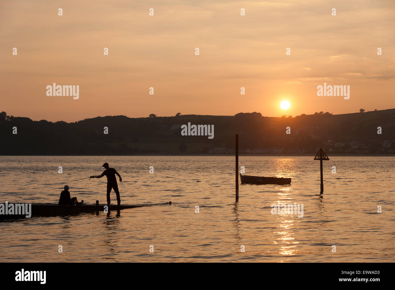 A silhouetted man casts a fishing line at sunset into the river Towy ...