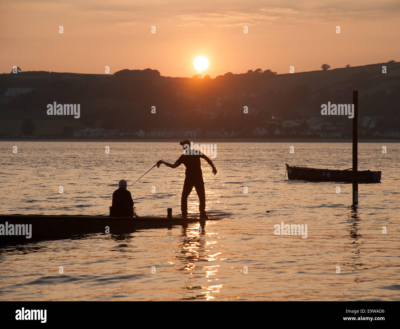 A silhouetted man casts a fishing line at sunset into the river Towy ...