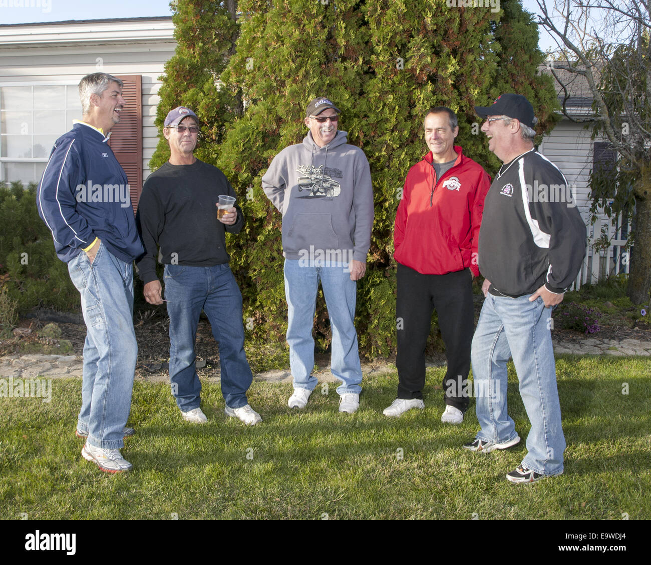 5 men are standing outside in a half circle. They are laughing. They ...