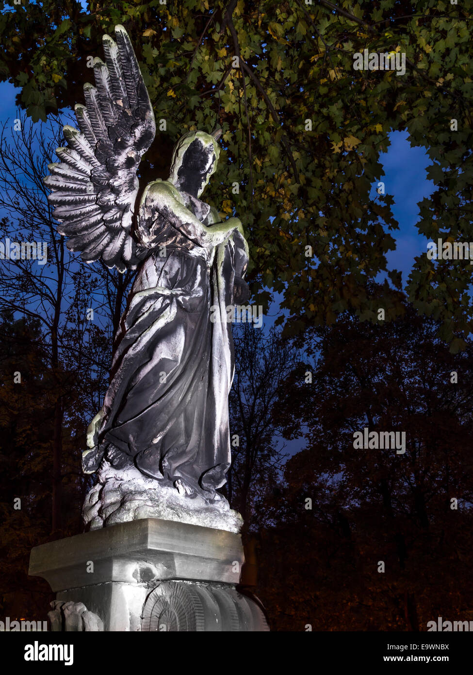 Stone statue of mourning angel on a tombstone against the dusk sky ...
