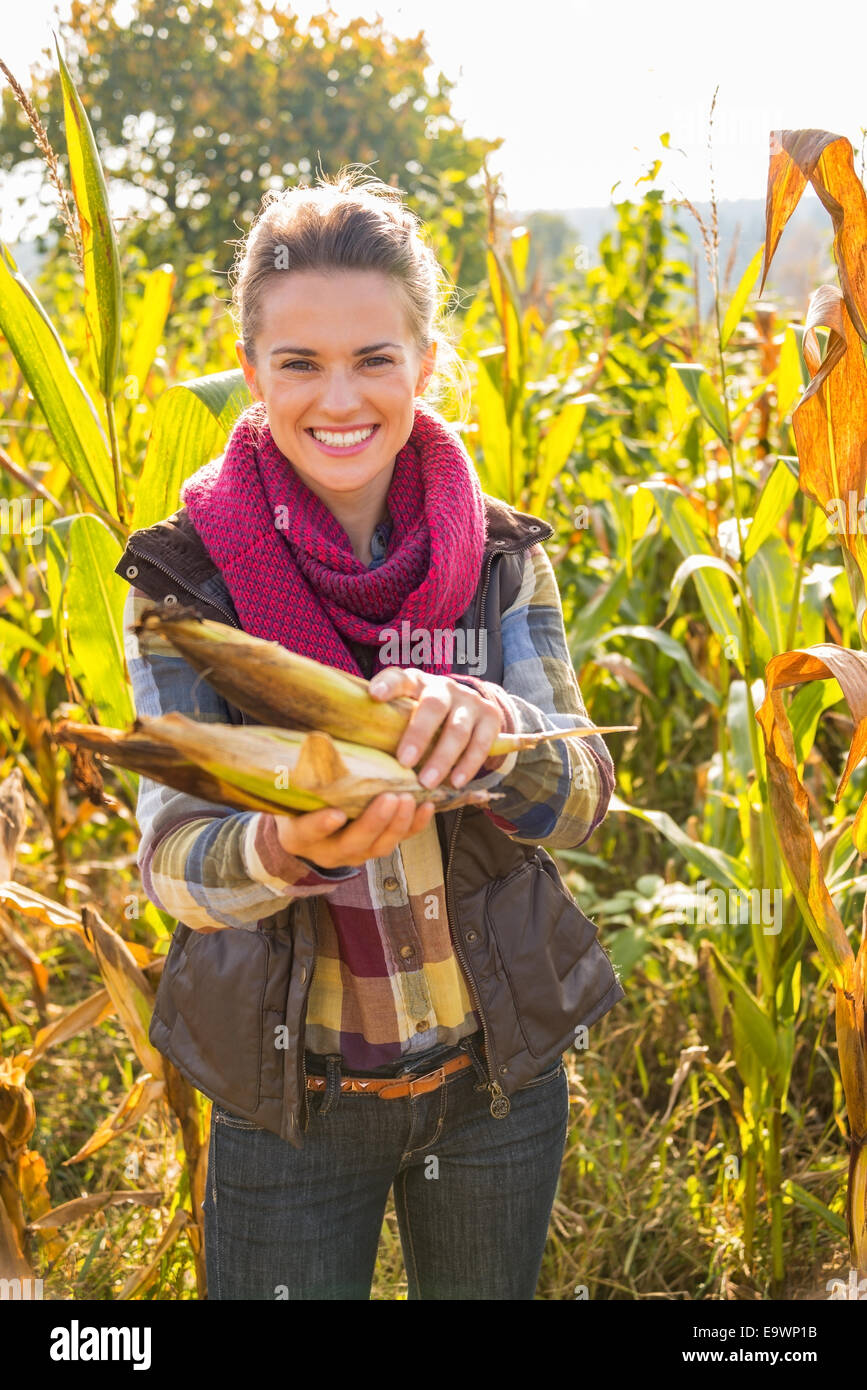 Happy young woman holding corn while standing in cornfield Stock Photo ...