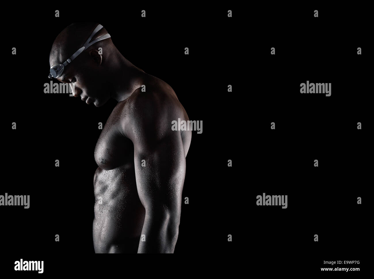 Side view of young male swimmer looking down over black background with ...