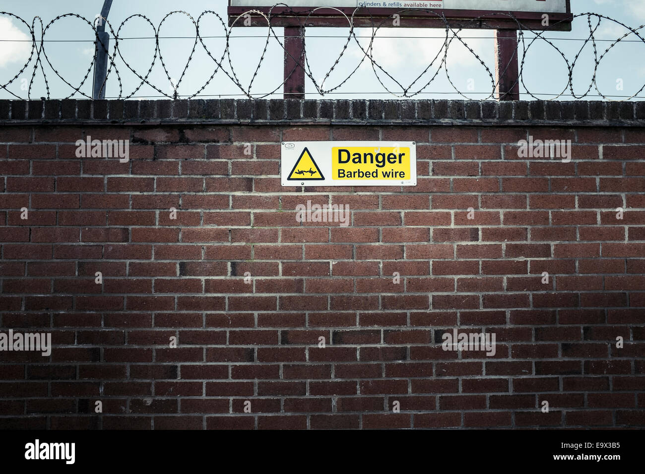Warning sign for 'Danger - barbed wire', fixed to a red brick wall ...