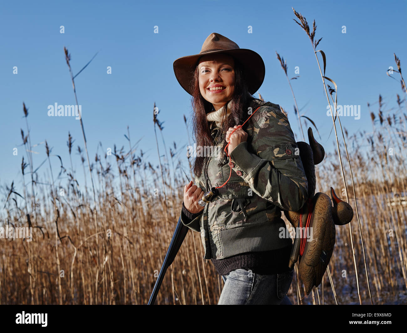 Waterfowl hunting, smiling female hunter carry a shotgun and a decoys ...