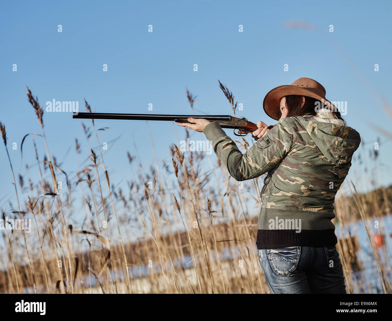Waterfowl hunting, female hunter use the shotgun, reeds and blue sky on ...