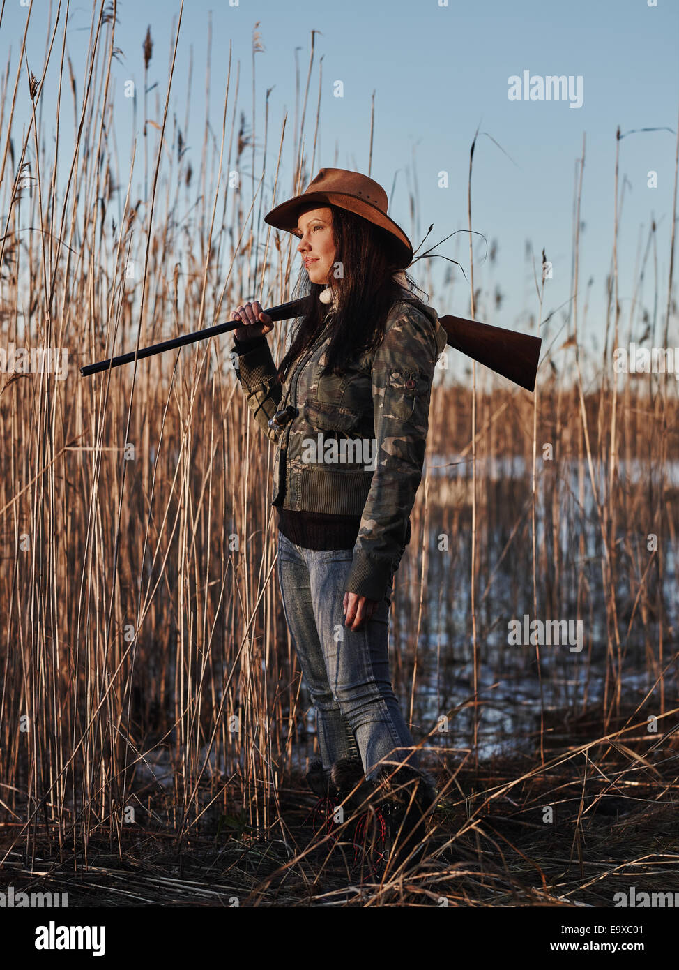Waterfowl hunting, female hunter carry a shotgun, reeds and blue sky on ...
