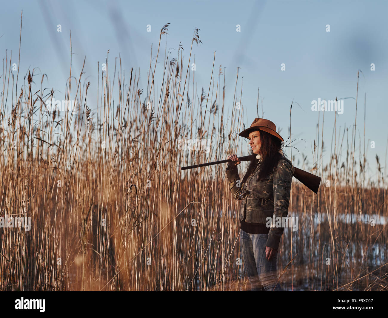 Waterfowl hunting, female hunter carry a shotgun, reeds and blue sky on ...