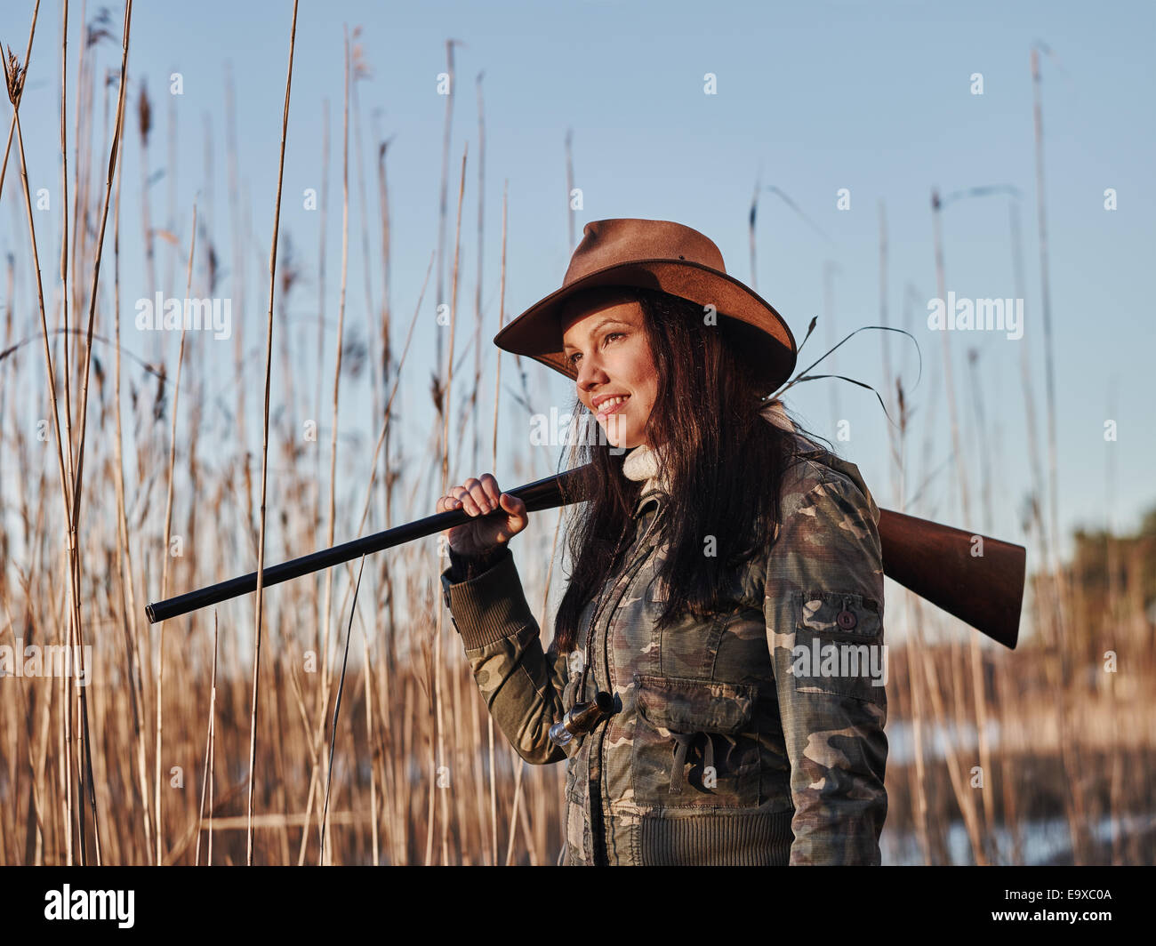 Waterfowl hunting, female hunter carry a shotgun, reeds and blue sky on ...