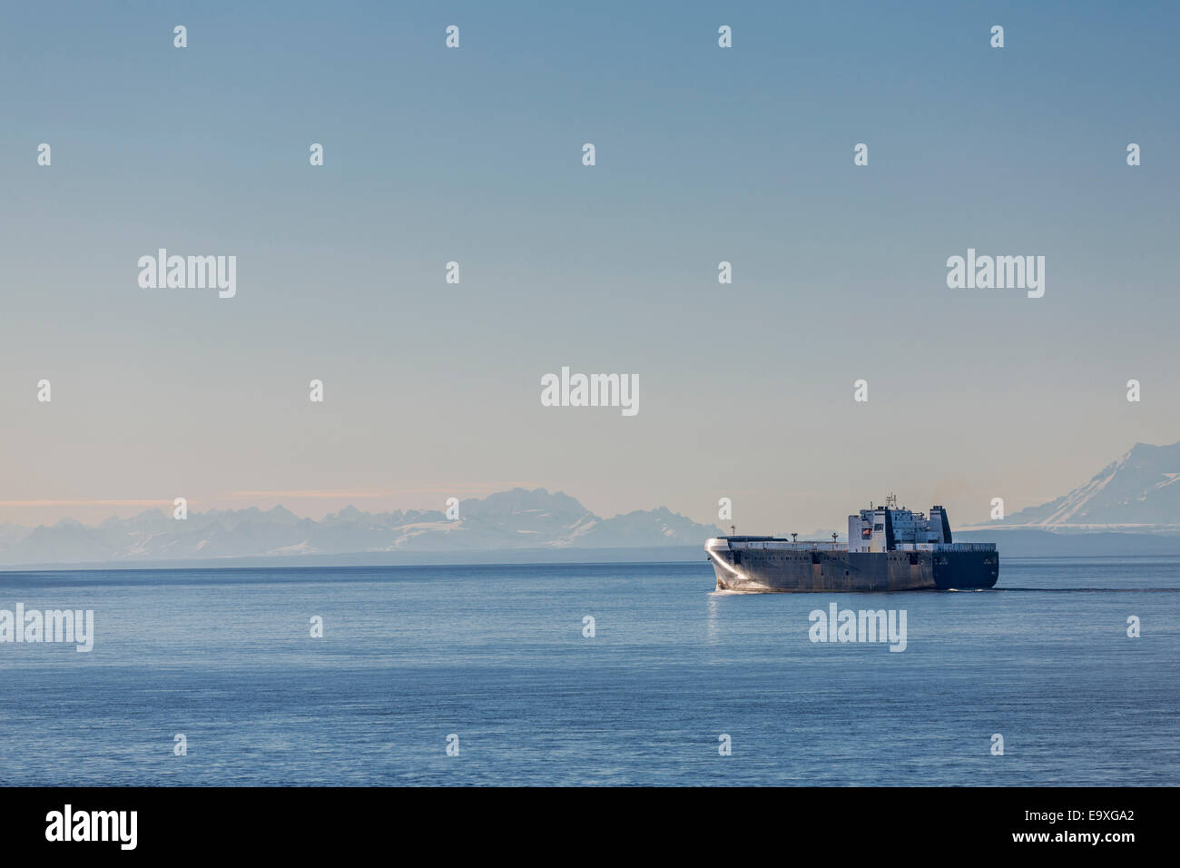 Cargo ship on the Pacific ocean with snowy mountains in the distance ...