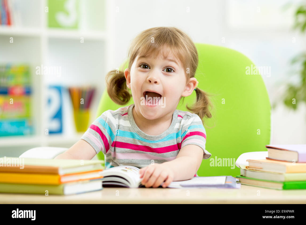 Happy kid reading book at table in nursery Stock Photo - Alamy
