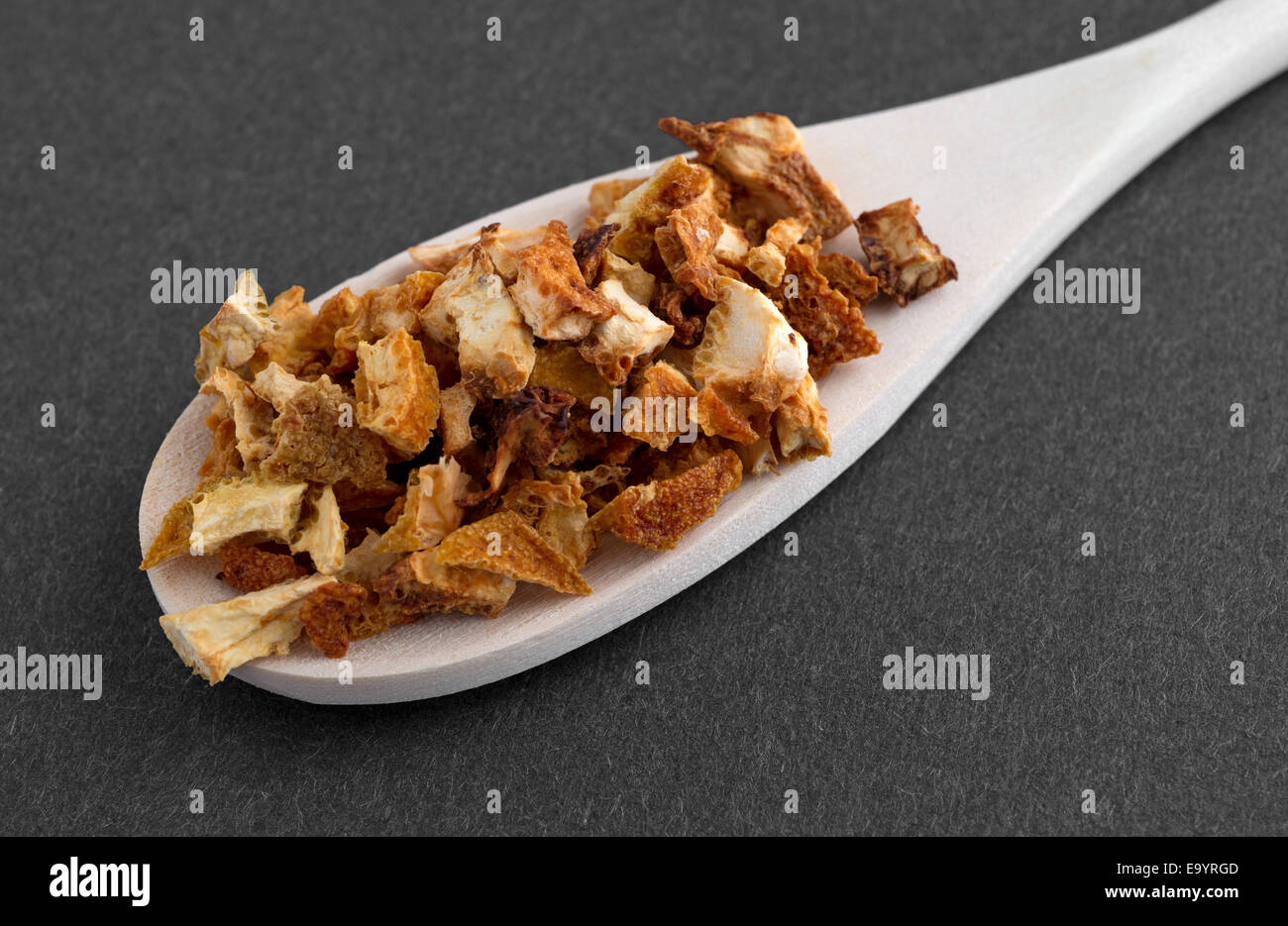 A small wood spoon filled with chopped orange peel rind on a dark ...