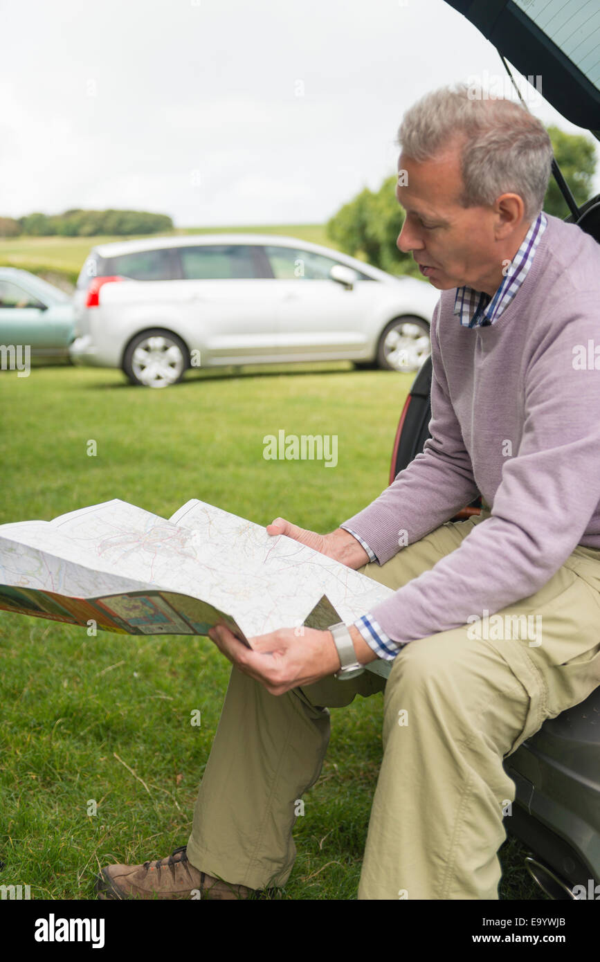 Man sitting on car boot reading map Stock Photo - Alamy