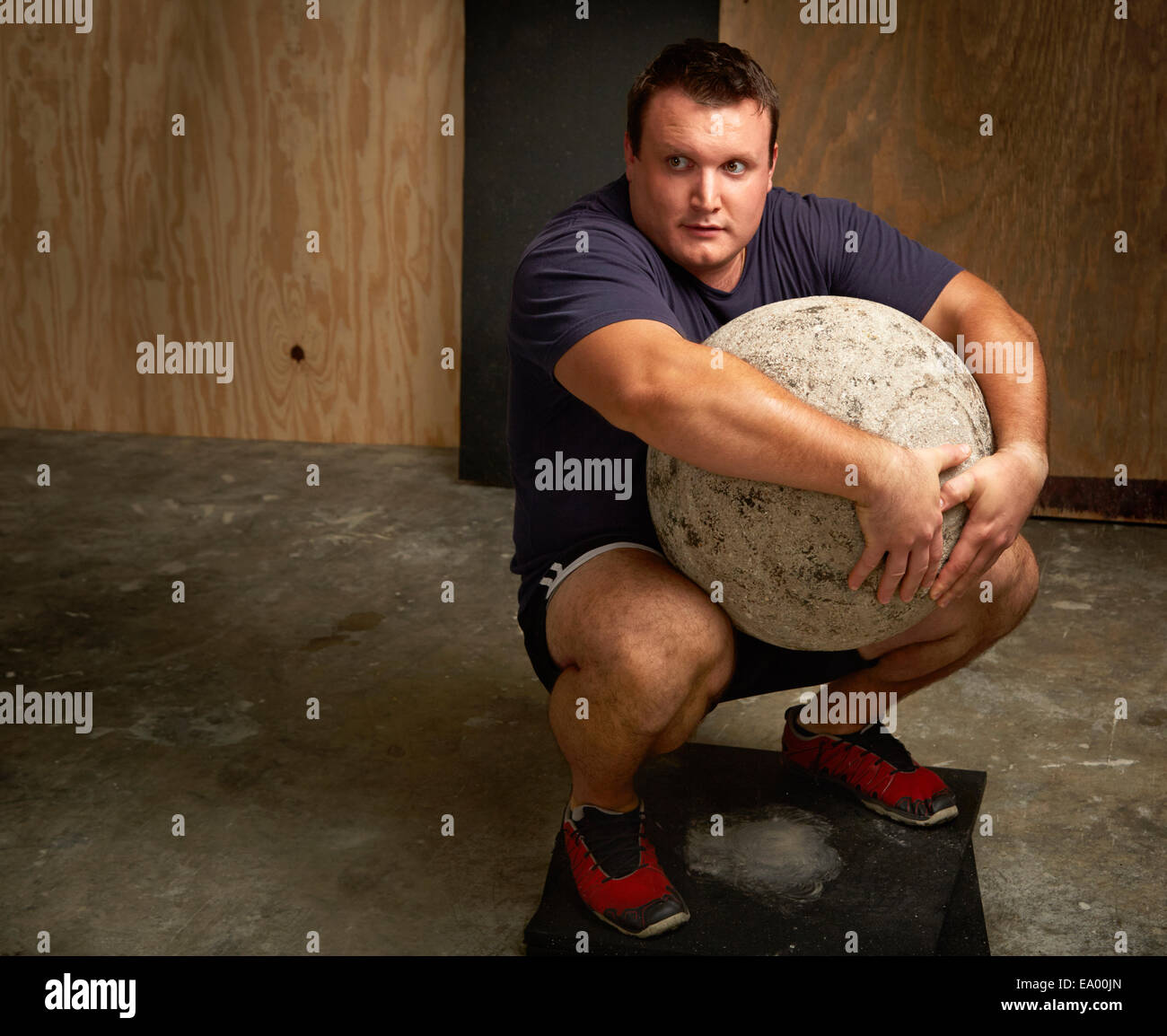 Portrait of young male weightlifter squatting with atlas ball in gym ...