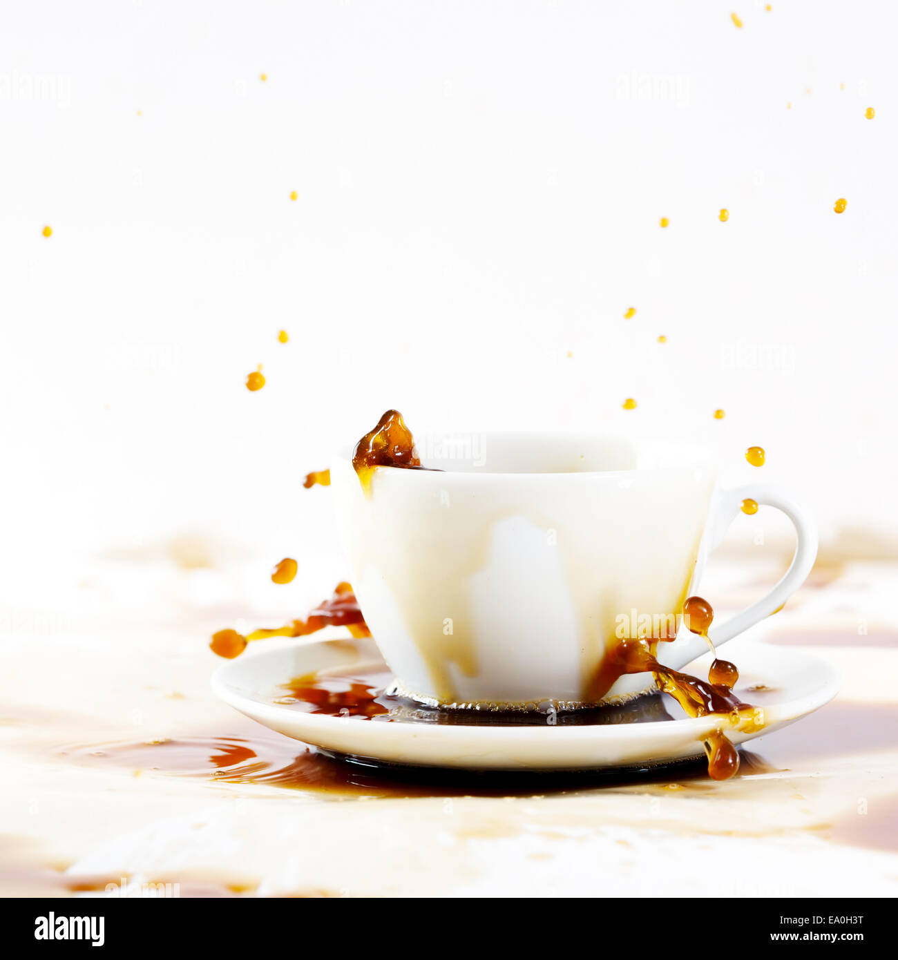 Cup of spilling coffee creating beautiful splash with stains on white ...