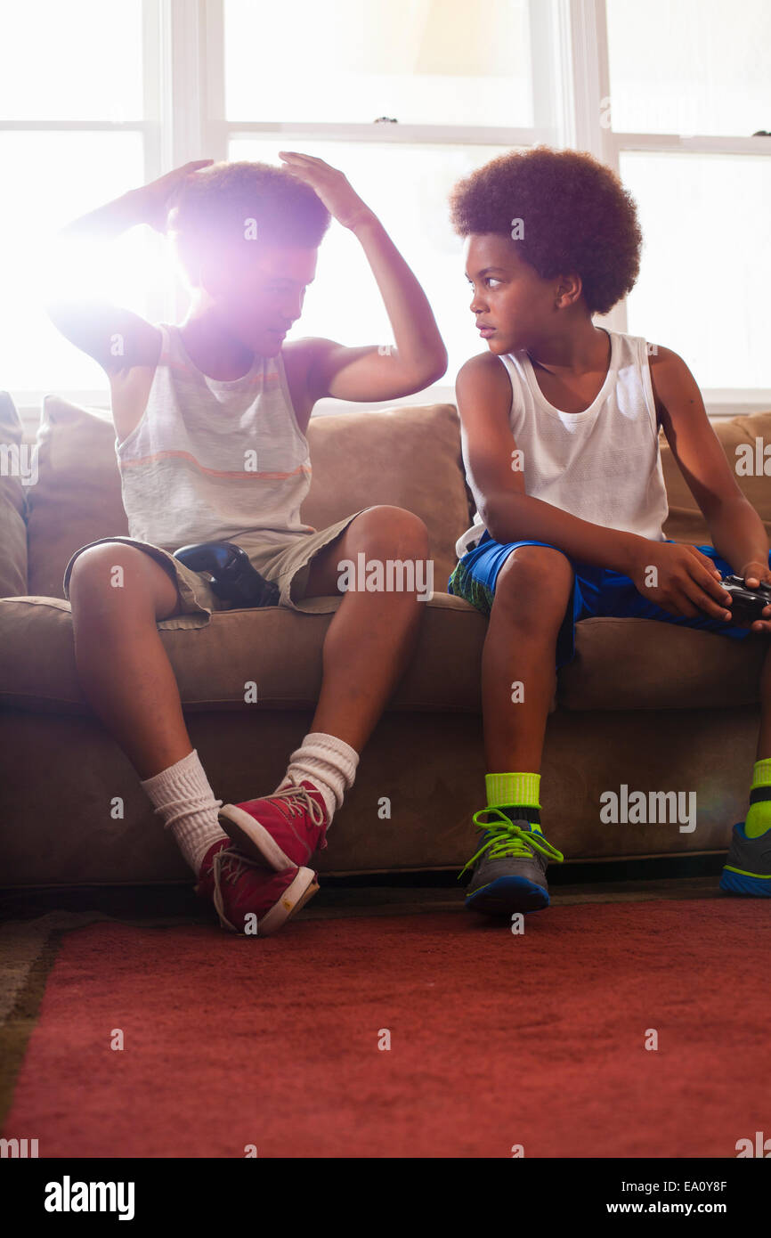 Two brothers with game controllers sitting on living room sofa Stock ...