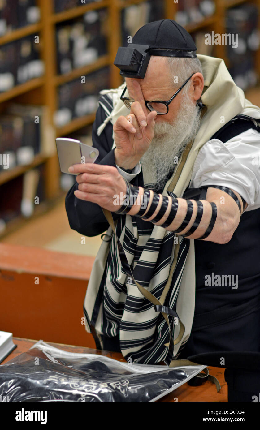 Using a small mirror an ultra religious Jew adjusting his phylacteries ...