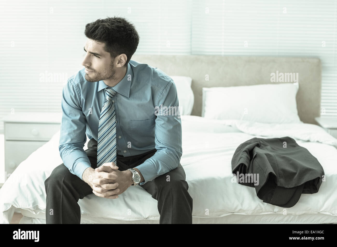 Handsome businessman sitting on bed thinking Stock Photo - Alamy