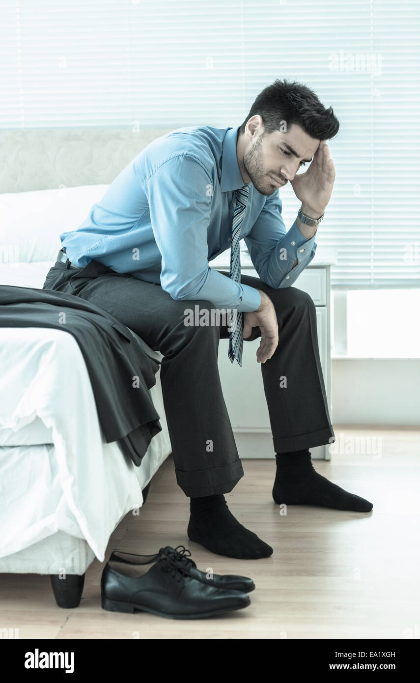 Wincing businessman sitting at edge of bed Stock Photo - Alamy