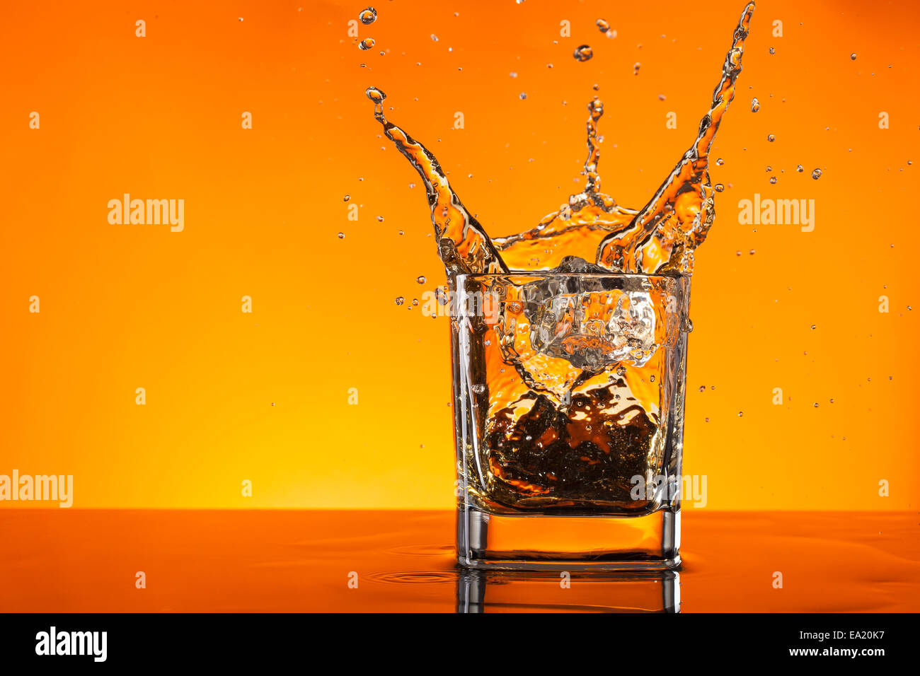 Whiskey shot splashing out of glass on orange background Stock Photo ...