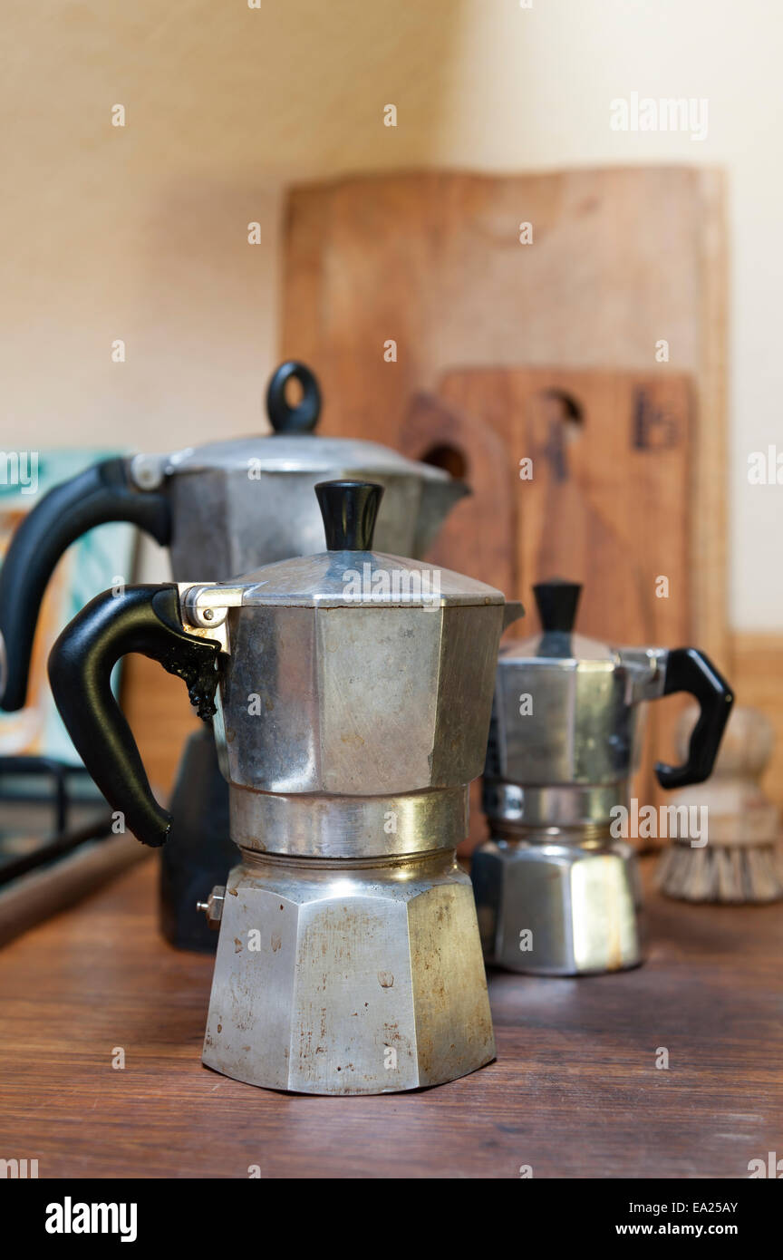 Three coffee percolators on wooden work surface with chopping boards in ...