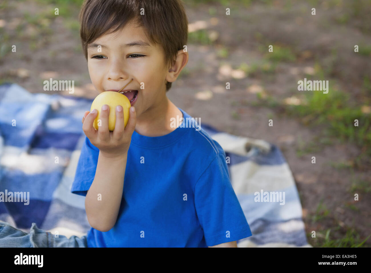 Cute young boy eating a fruit in park Stock Photo - Alamy