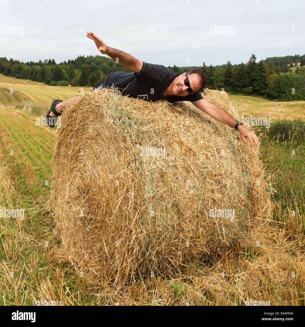 A man lays in a silly pose on top of a large hay bale; Kensington ...