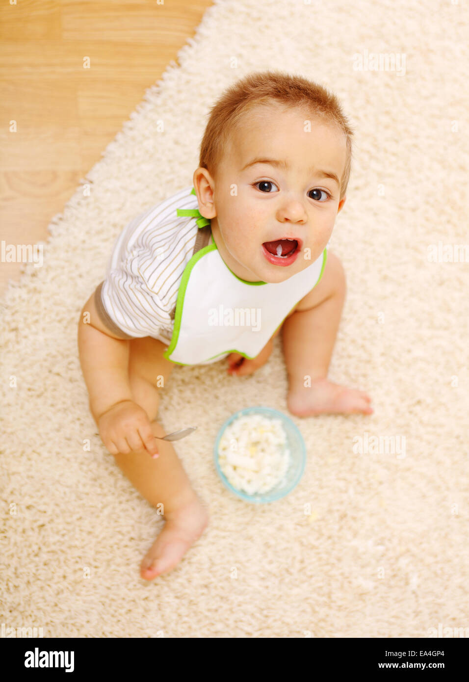 Baby boy sitting alone on shaggy carpet and eating Stock Photo - Alamy