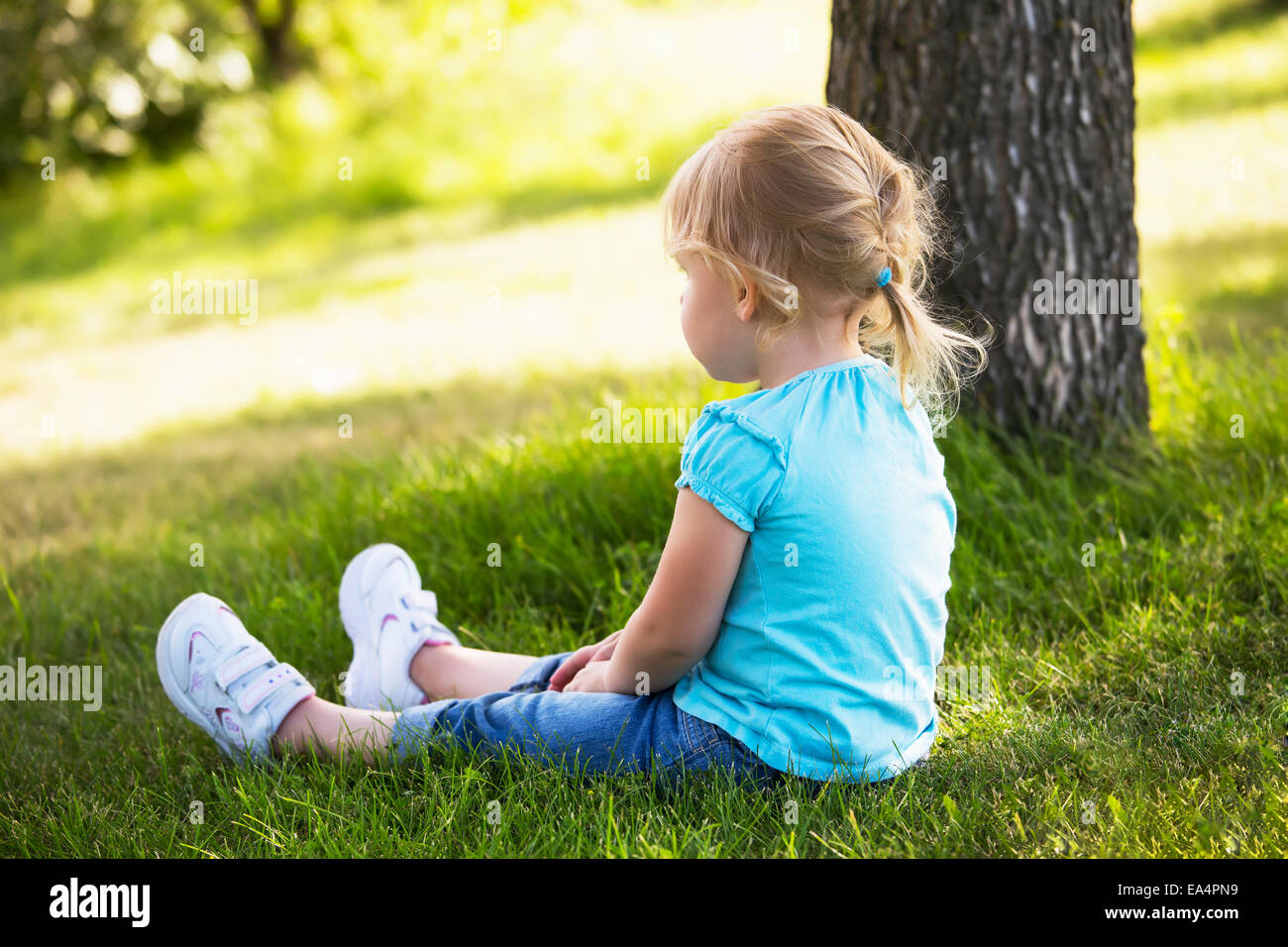 Toddler girl sitting in a park beside a tree; Edmonton, Alberta, Canada ...