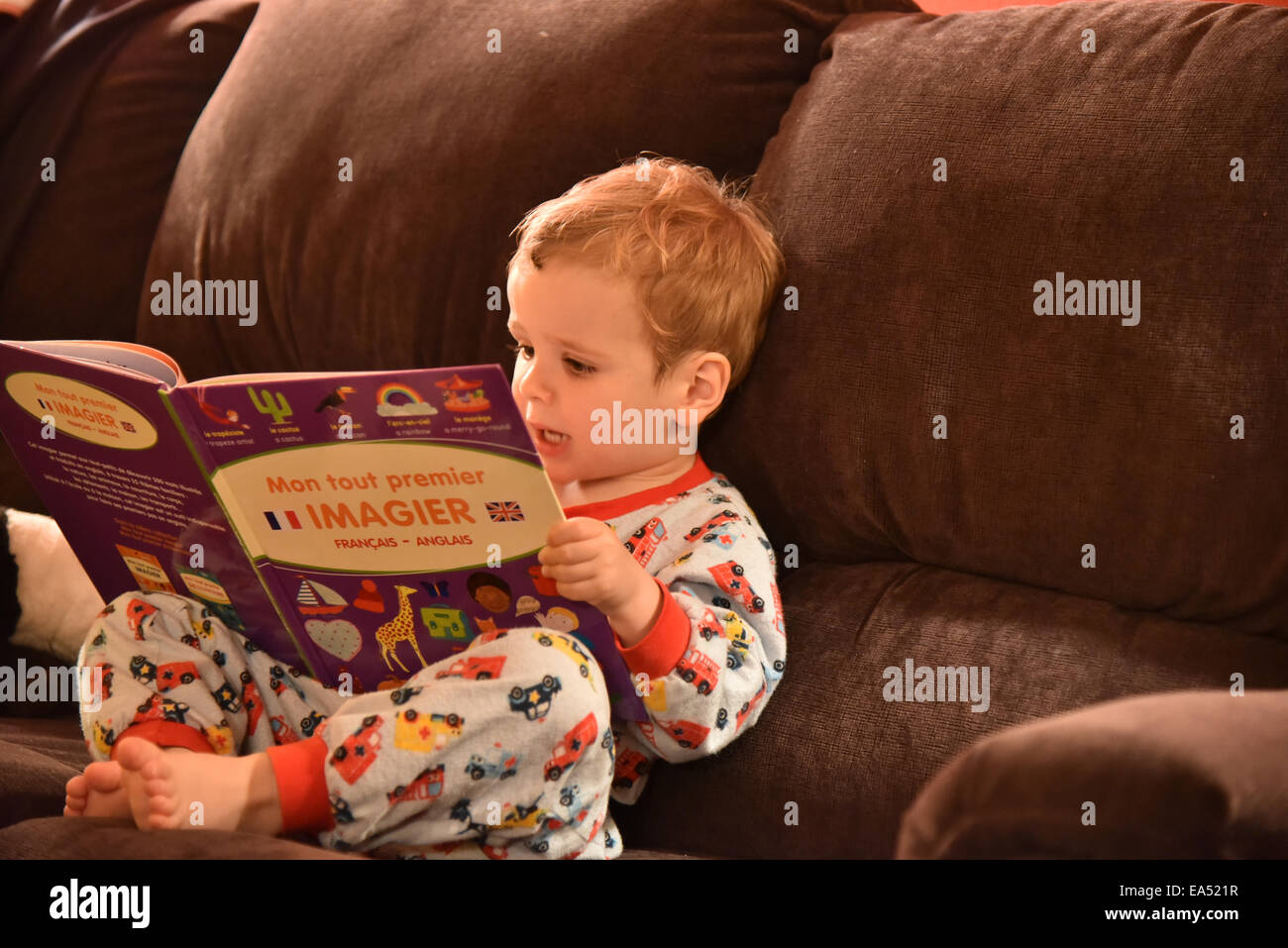 A young boy (two and a half years old) in pyjamas sat on a sofa reading ...