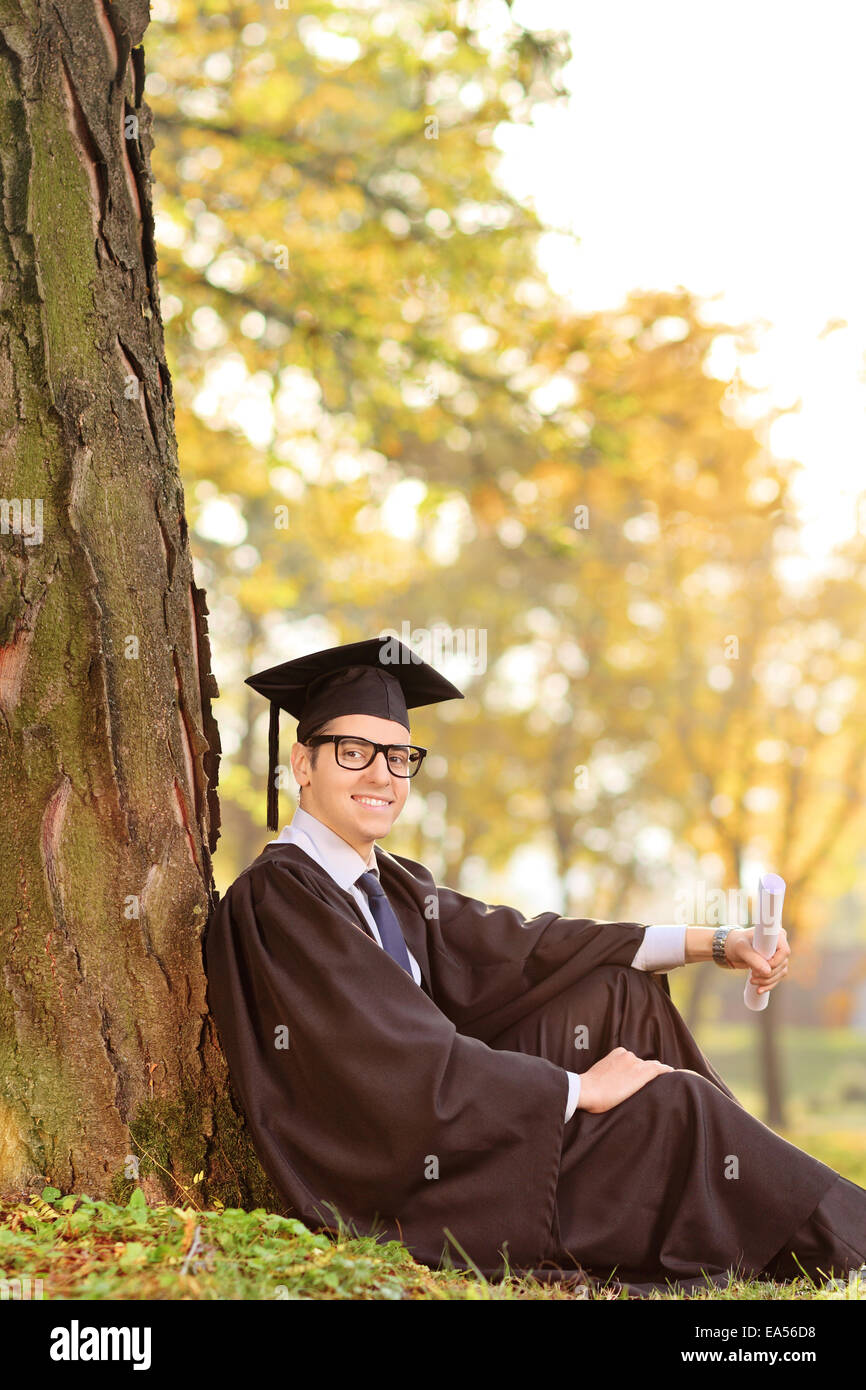 Vertical shot of a college graduate sitting by a tree in a park Stock ...
