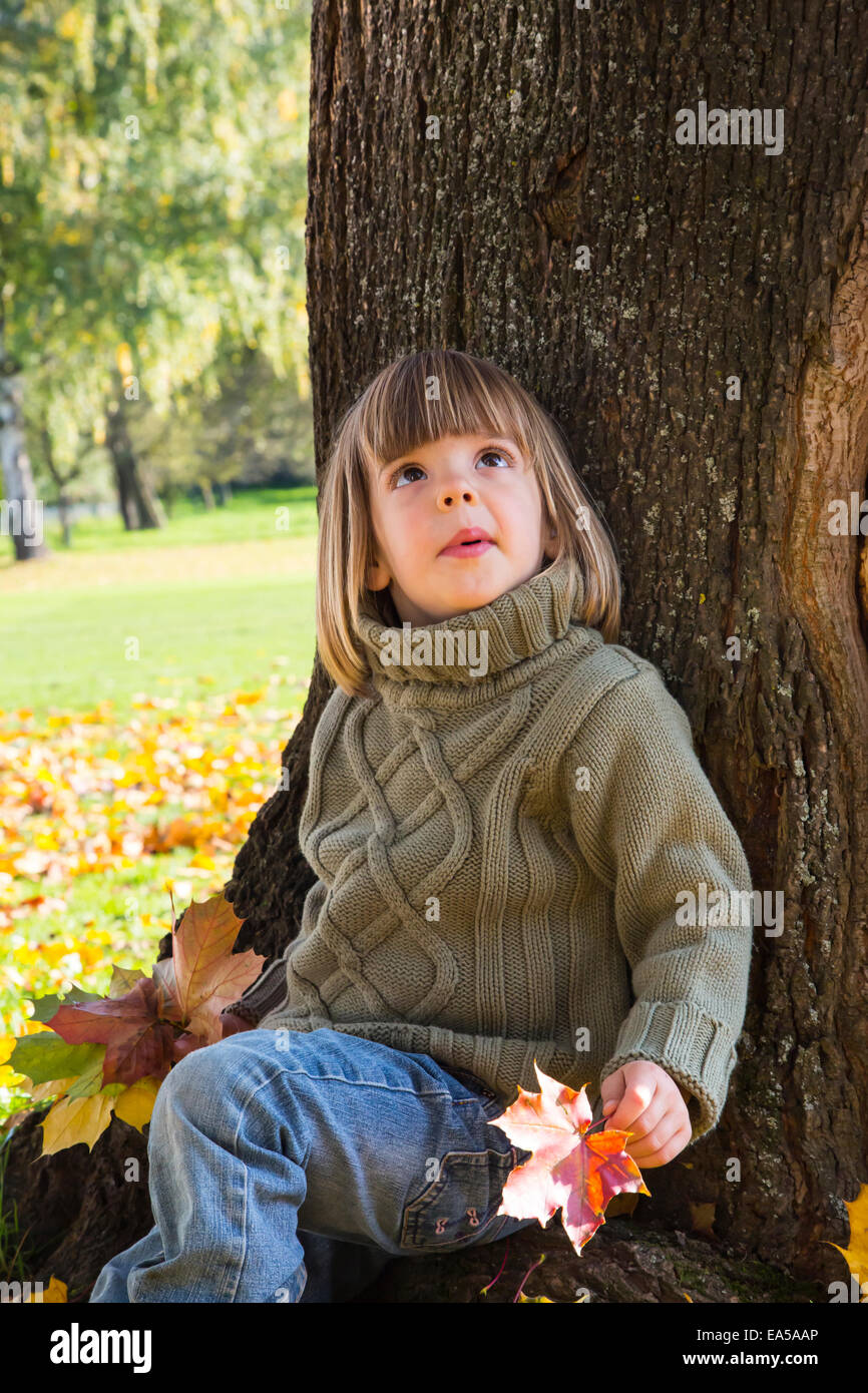 Little girl leaning at tree trunk looking up Stock Photo - Alamy