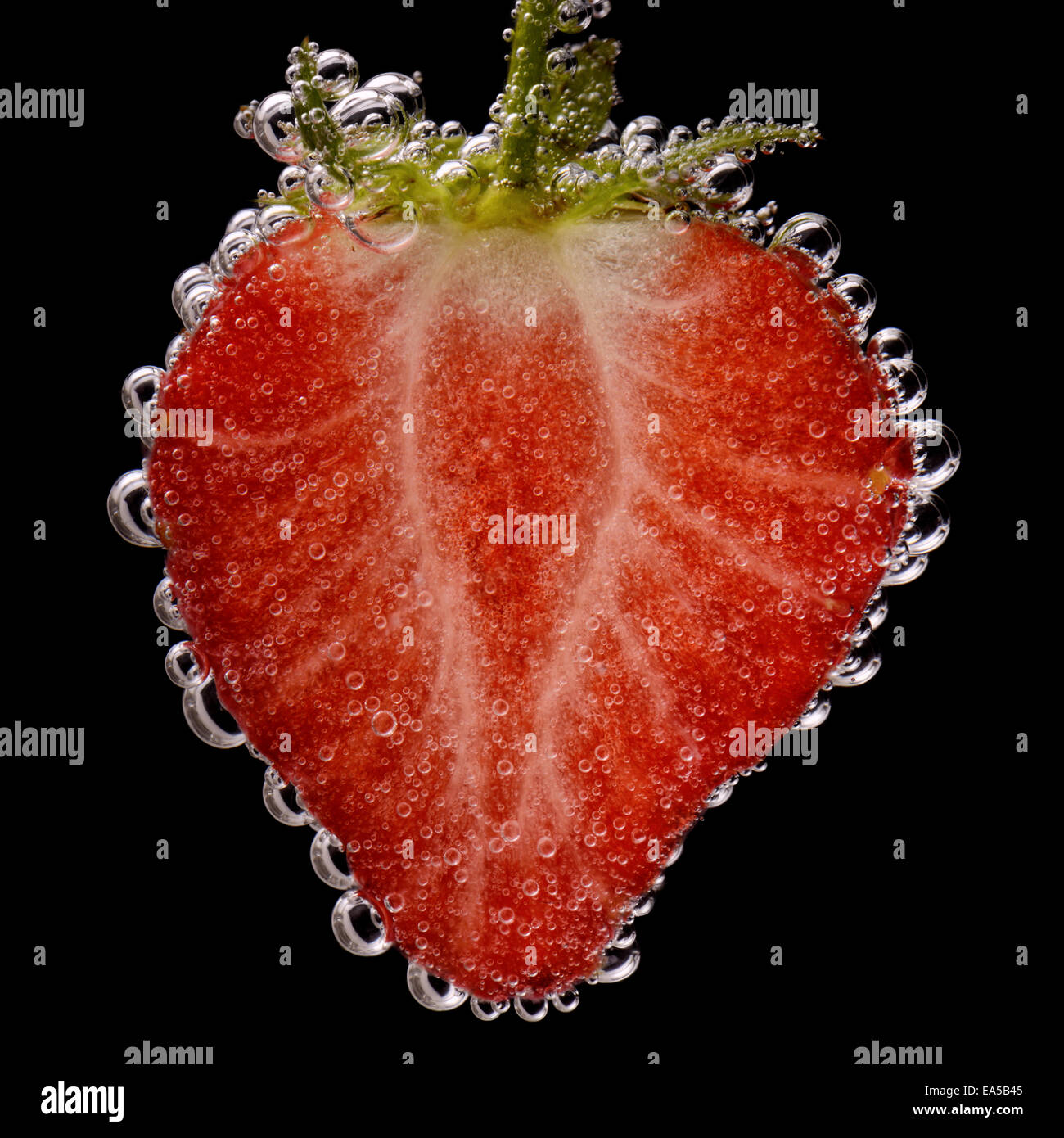 Sliced strawberry with air bubbles in front of black background, close ...