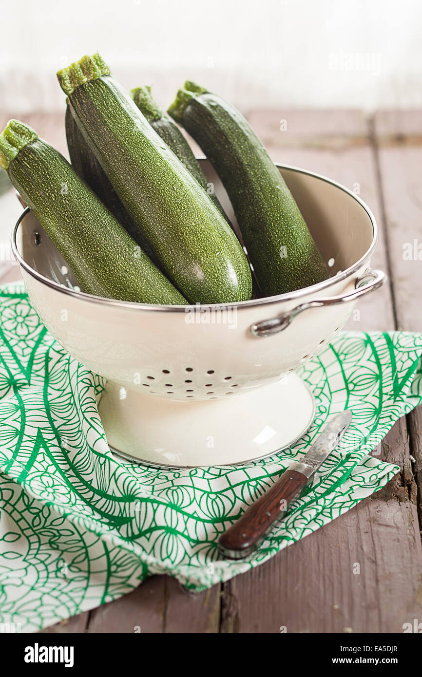 Colander of courgettes and a knife on cloth and wood Stock Photo - Alamy