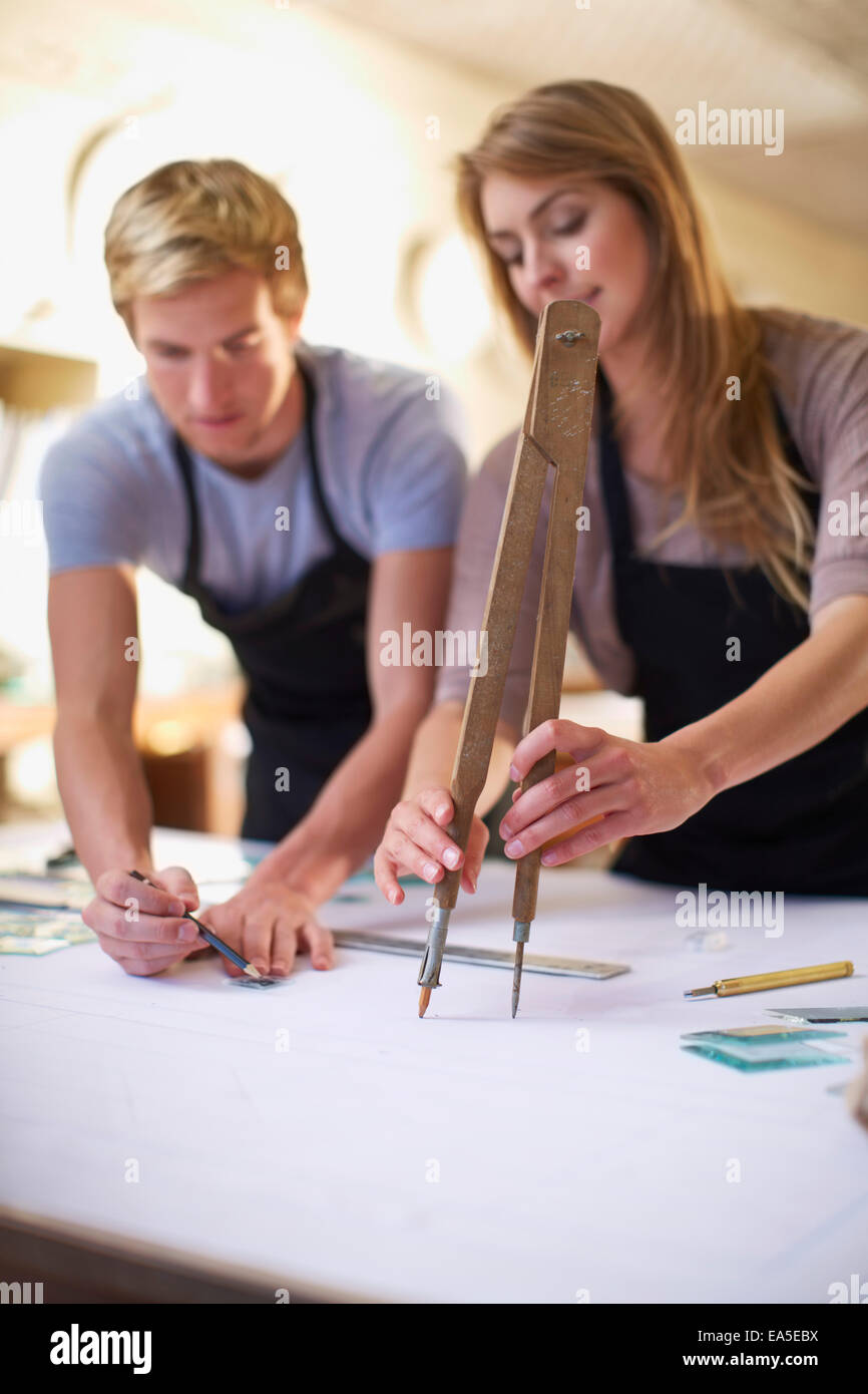 Couple in a workshop manufacturing stained glass with large compasses ...