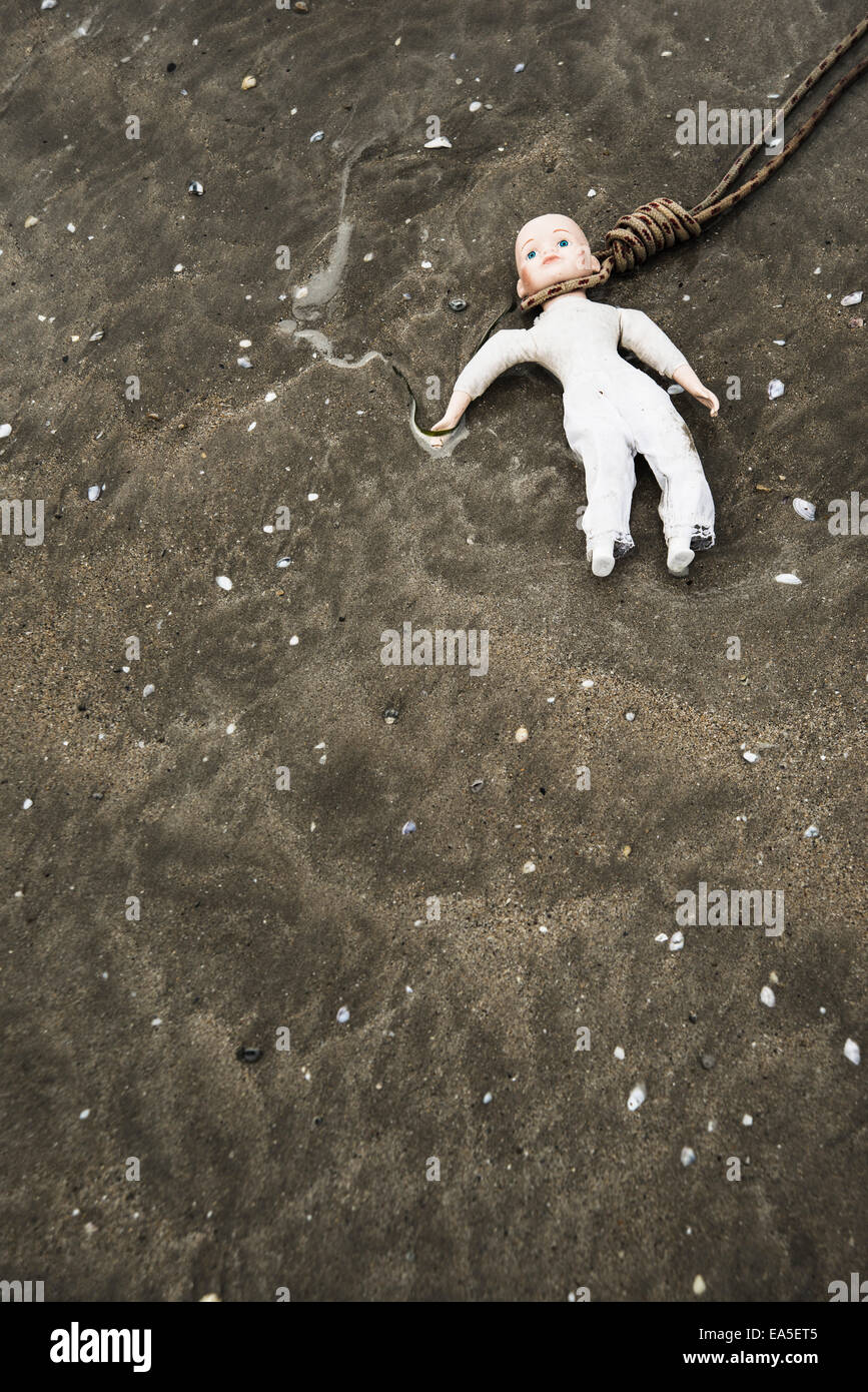 Doll lying on wet sandy beach with rope on the neck Stock Photo - Alamy