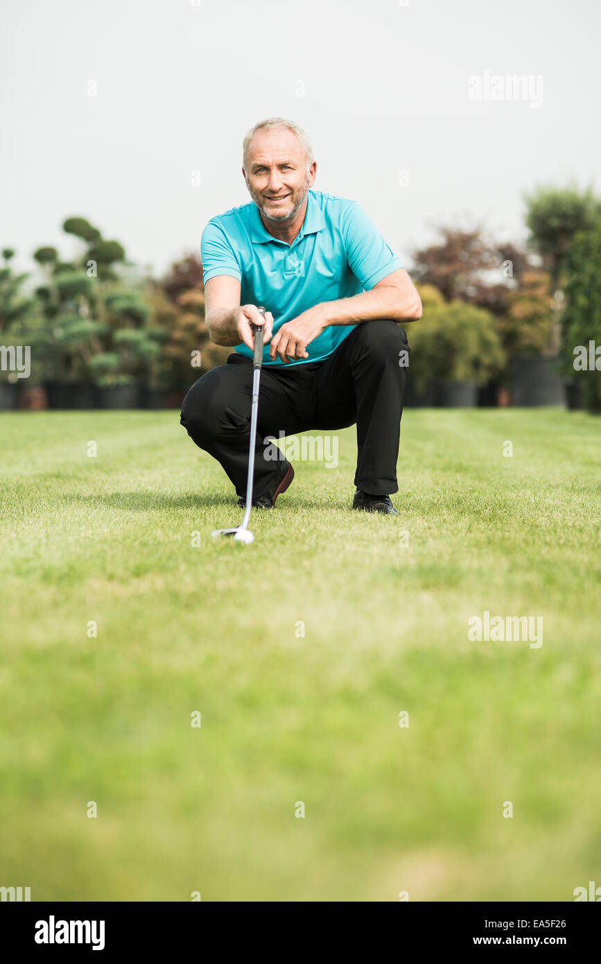Golf player crouching on turf looking at golf ball Stock Photo - Alamy