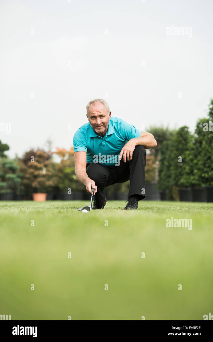 Golf player crouching on turf looking at golf ball Stock Photo - Alamy