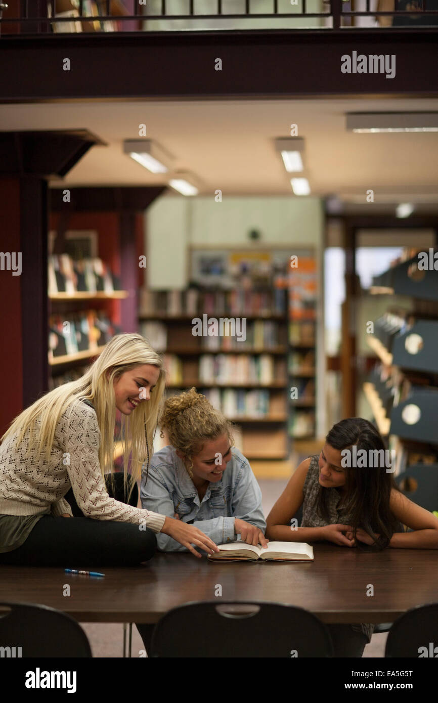 Three female students in a library reading book Stock Photo - Alamy