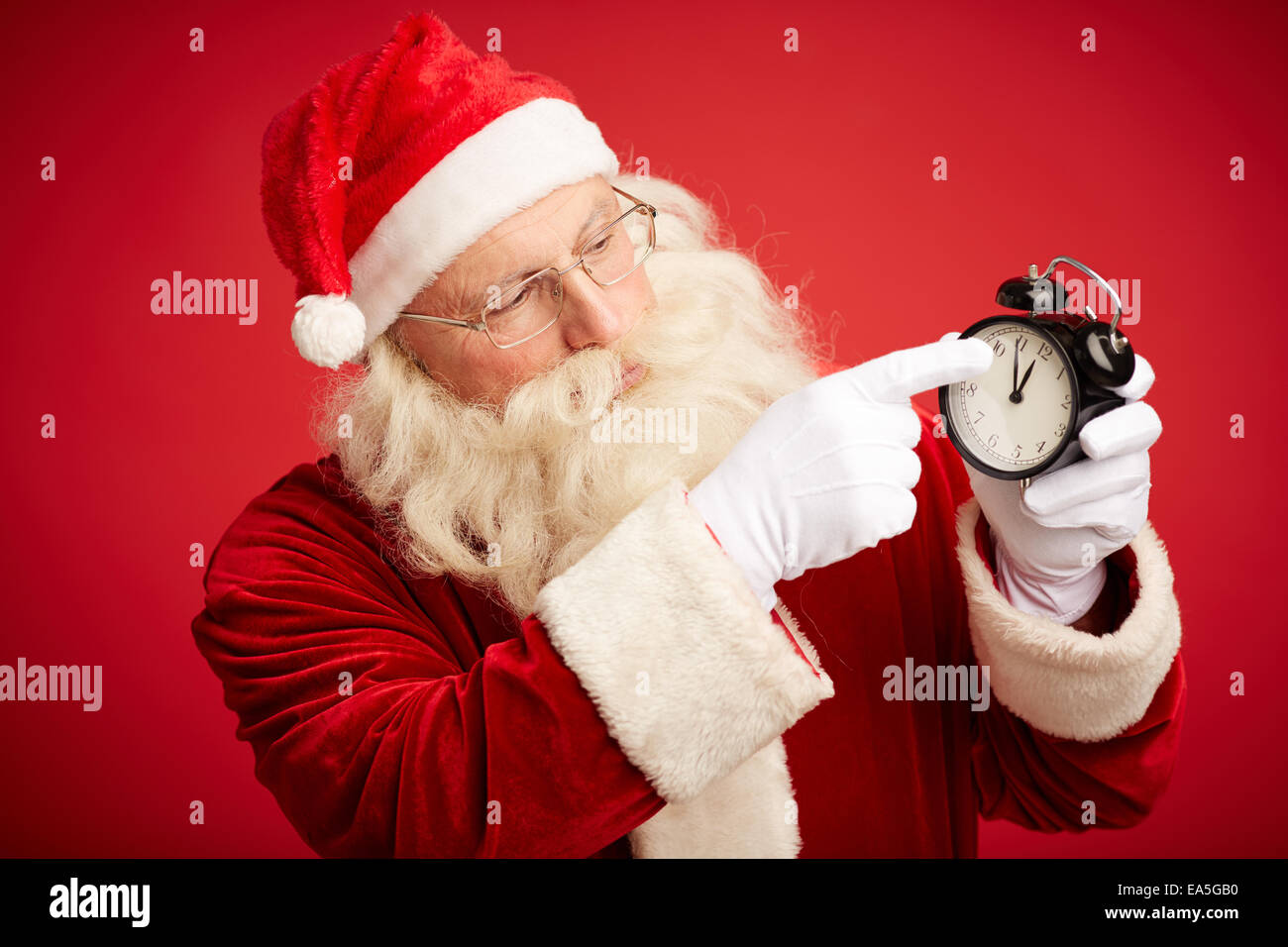 Santa Claus pointing at alarm clock showing five minutes to twelve ...