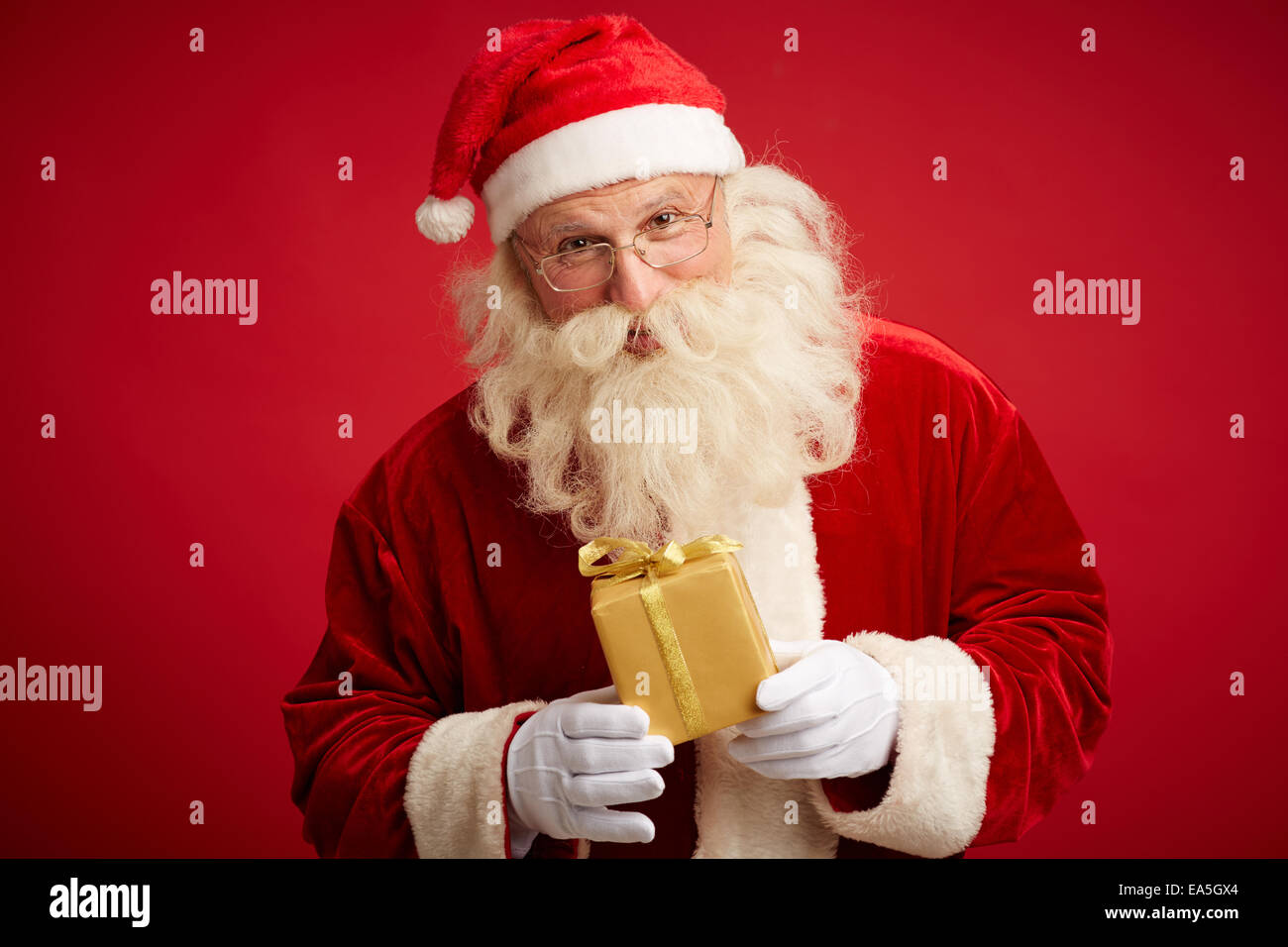 Kind Santa Claus holding small package wrapped in golden paper and ...