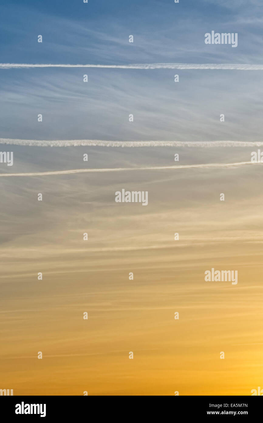 Sunset sky, orange fading to blue; with wispy clouds and contrails ...