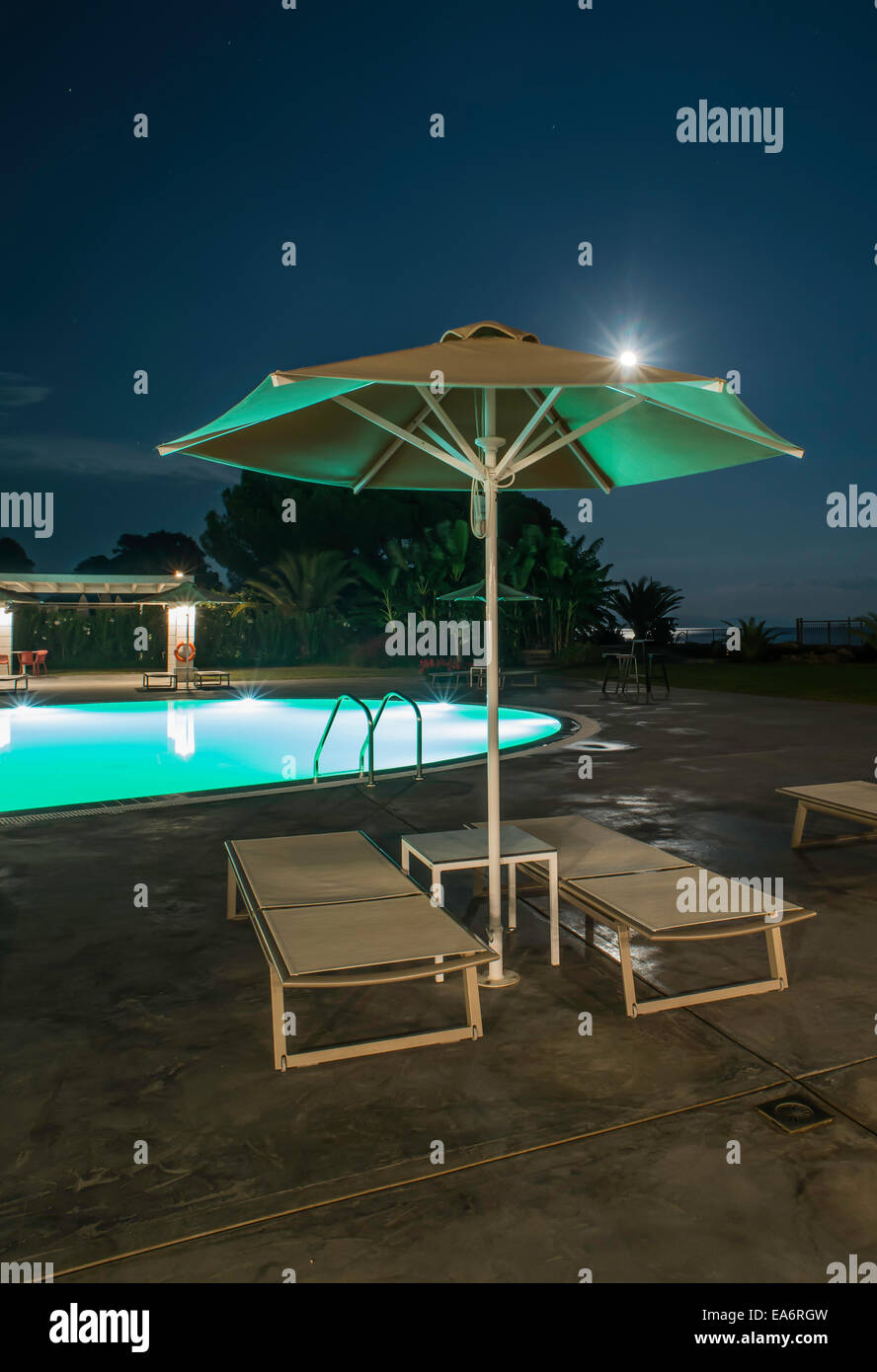 Pool, sunbeds and umbrellas at night. Night lights Stock Photo - Alamy