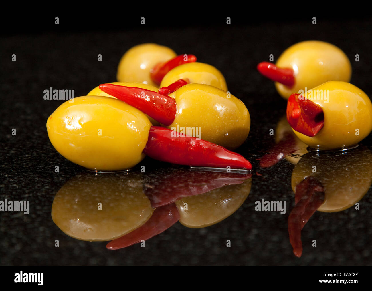 Red chilli stuffed olives in olive oil on a black granite base Stock ...