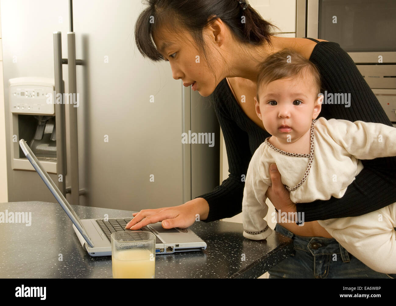 busy young korean asian mum using laptop computer in modern kitchen ...