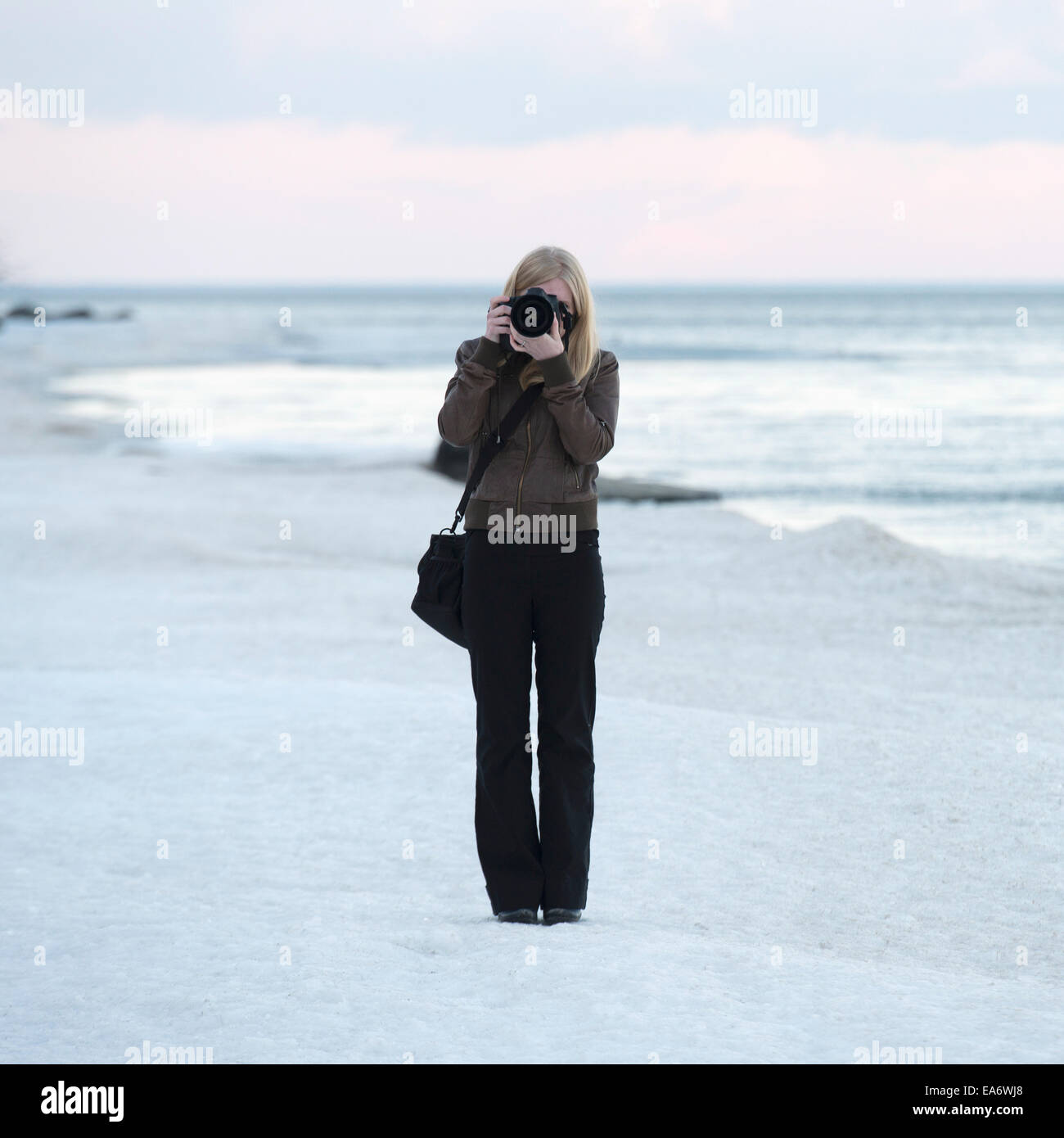 A woman stands on the beach with a camera pointed at the camera ...