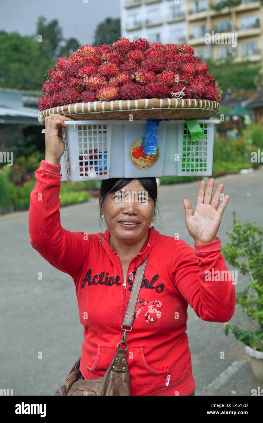 Smiling Filipino woman carries a basket of rambutan fruit on her head ...