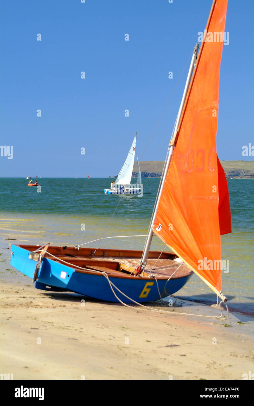 red sailed dinghy on the beach at low tide with yacht sailing across ...
