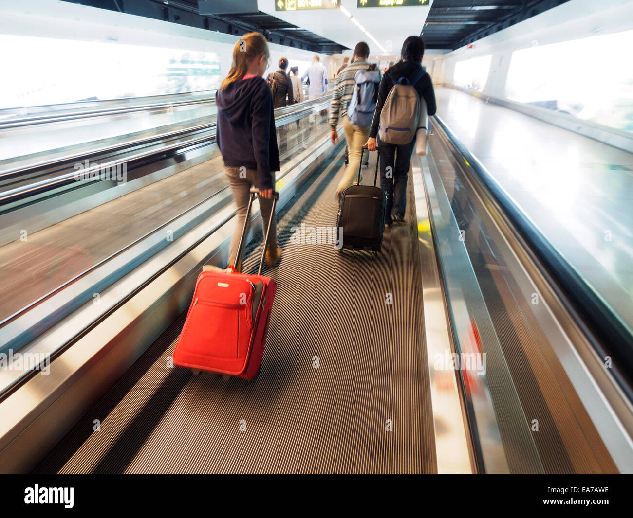Rear view of people with rolling suitcases on a moving walkway at the ...
